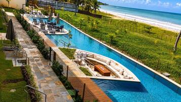 Uma área de piscina com barco, espreguiçadeiras e vista para a praia.