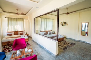 Quarto de hotel com duas camas, um espelho grande, um espaço de estar com uma mesa e um ventilador de teto.