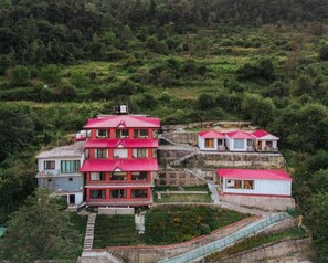 Um edifício de vários andares com telhado vermelho, rodeado por vegetação exuberante e terrenos em terraços.