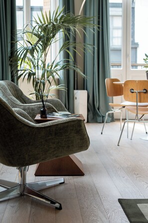 Uma sala de estar moderna com uma poltrona verde, uma mesa de centro de madeira, uma planta em vaso e piso de madeira.