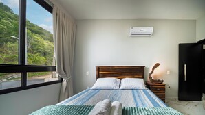 Quarto de hotel com cama, janela com cortinas, mesa de cabeceira com abajur e ar condicionado na parede.