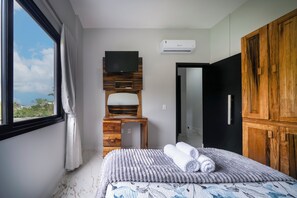Quarto com uma cama, uma escrivaninha de madeira, uma televisão e um guarda-roupa.