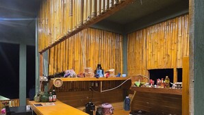 Uma área de bar com um balcão de madeira comprido, banquetas e painéis de bambu nas paredes.