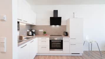 Uma cozinha moderna com armários brancos, coifa preta e forno de aço inoxidável.