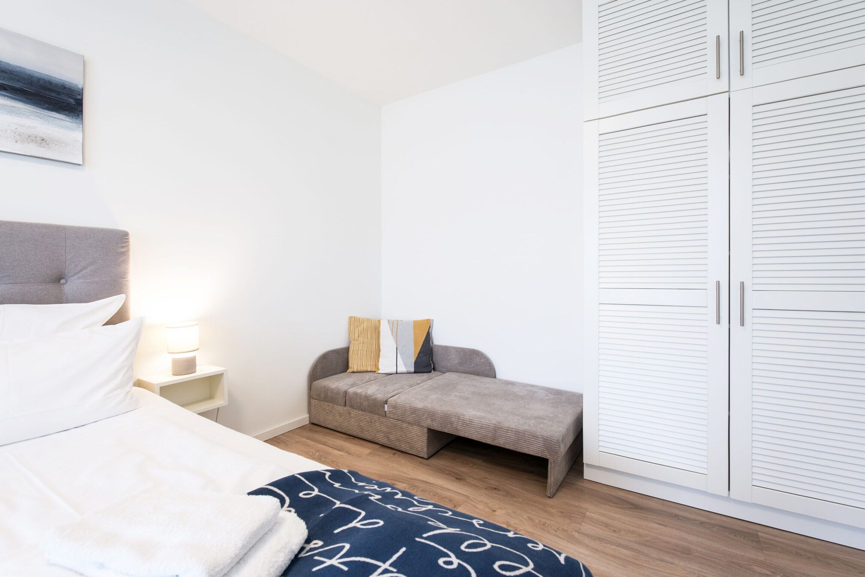 Quarto com cama, mesa de cabeceira com luminária, sofá e guarda-roupa.