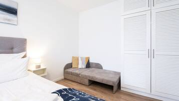 Quarto com cama, mesa de cabeceira com luminária, sofá e guarda-roupa.