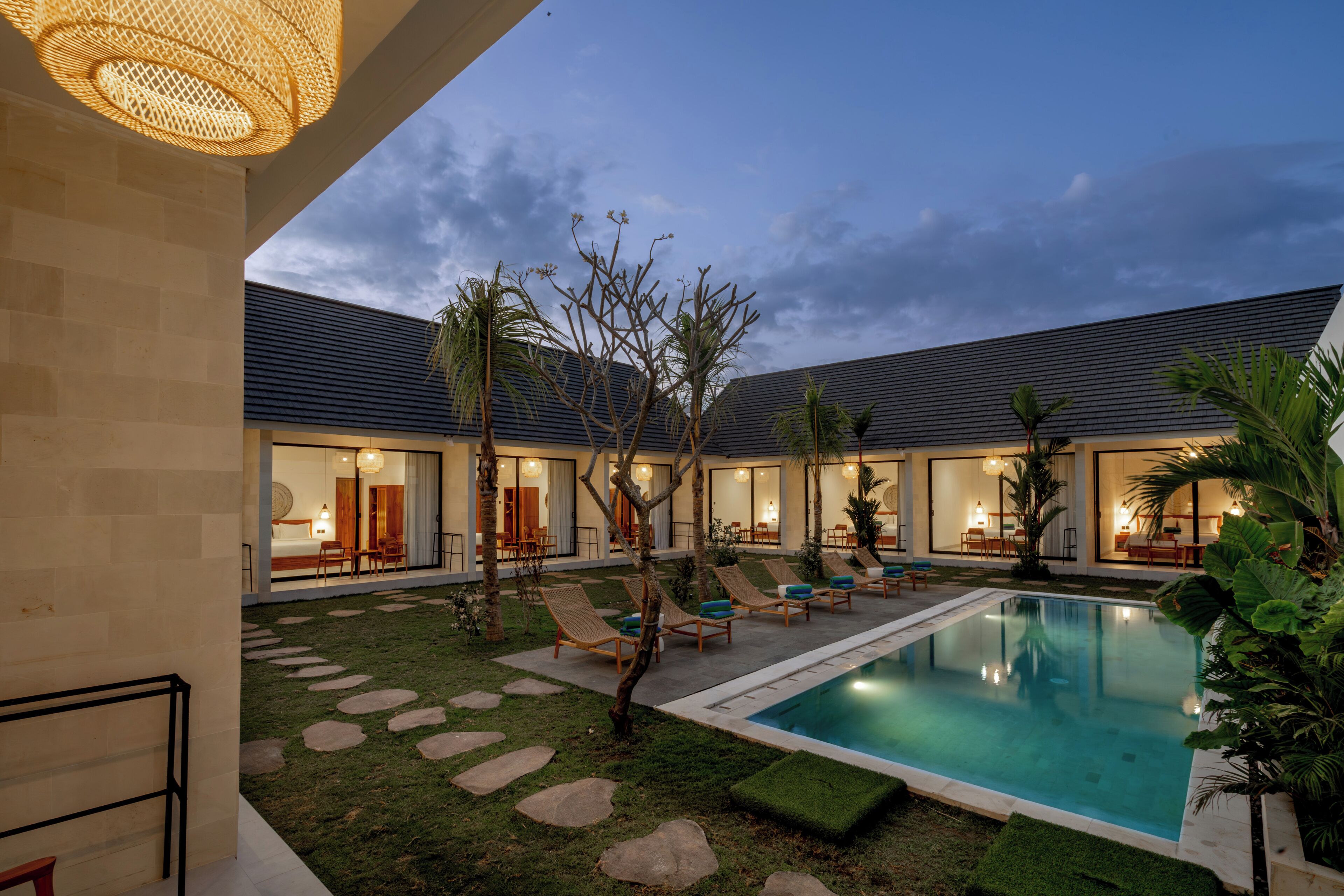 Uma área ao lado da piscina com espreguiçadeiras, piscina e um edifício com amplas janelas e portas.