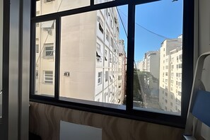 Uma janela com vista para edifícios altos, uma cortina e uma parede.