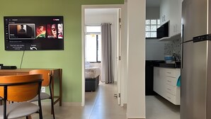 Uma cozinha moderna com micro-ondas embutido, uma área de jantar com mesa e cadeiras de madeira, e uma TV na parede exibindo um filme.