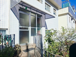 A modern building with a glass entrance, a green garden hose, and a metal railing.