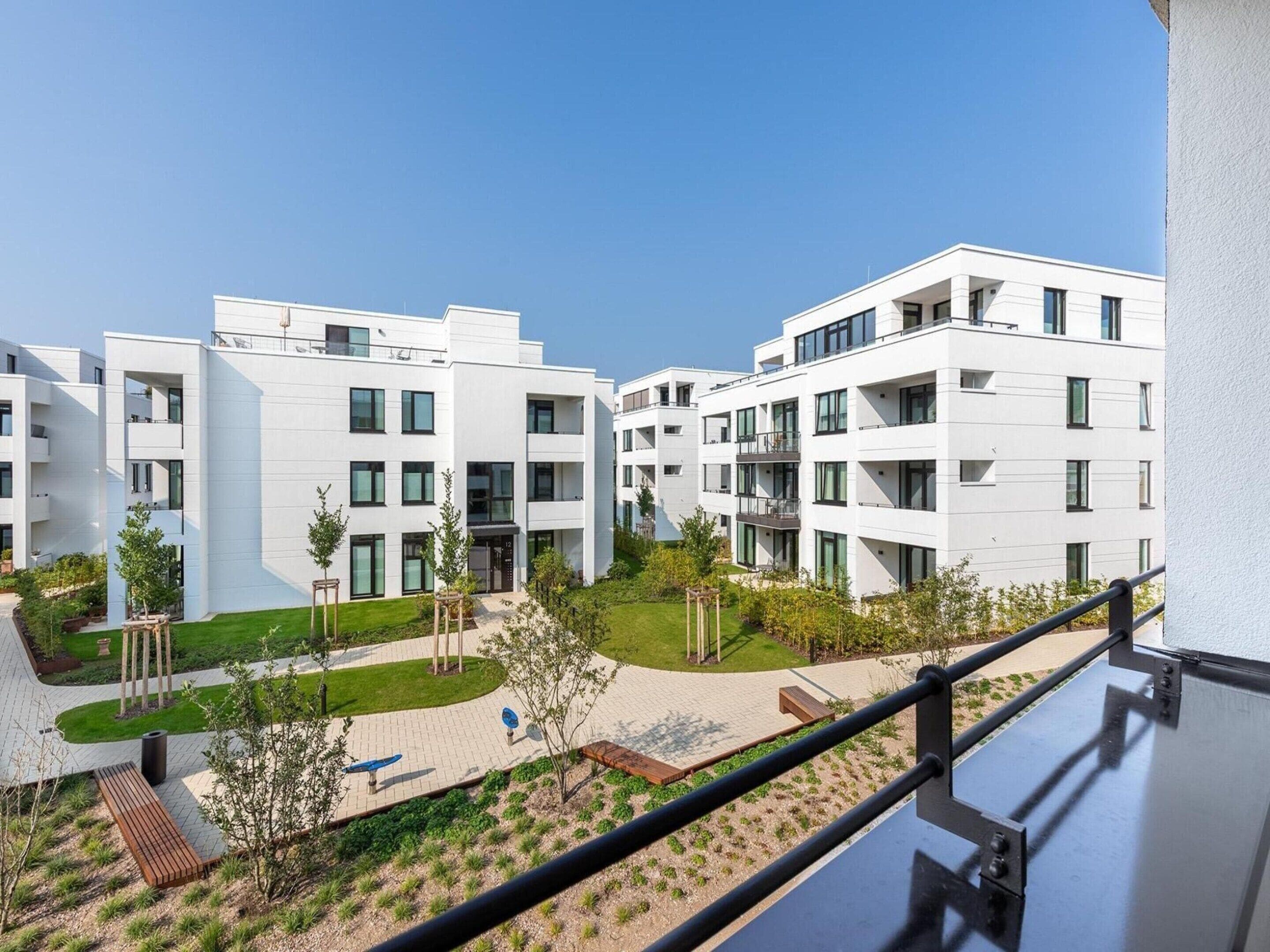 Um edifício residencial moderno com várias varandas, um pátio ajardinado e céu claro.
