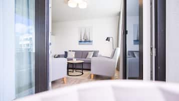 Uma sala de estar moderna com um sofá, duas poltronas, uma mesa de centro e uma pintura de barcos a vela na parede.