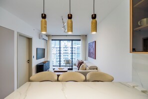 Quarto de hotel moderno com uma grande janela, área de jantar e um sofá.