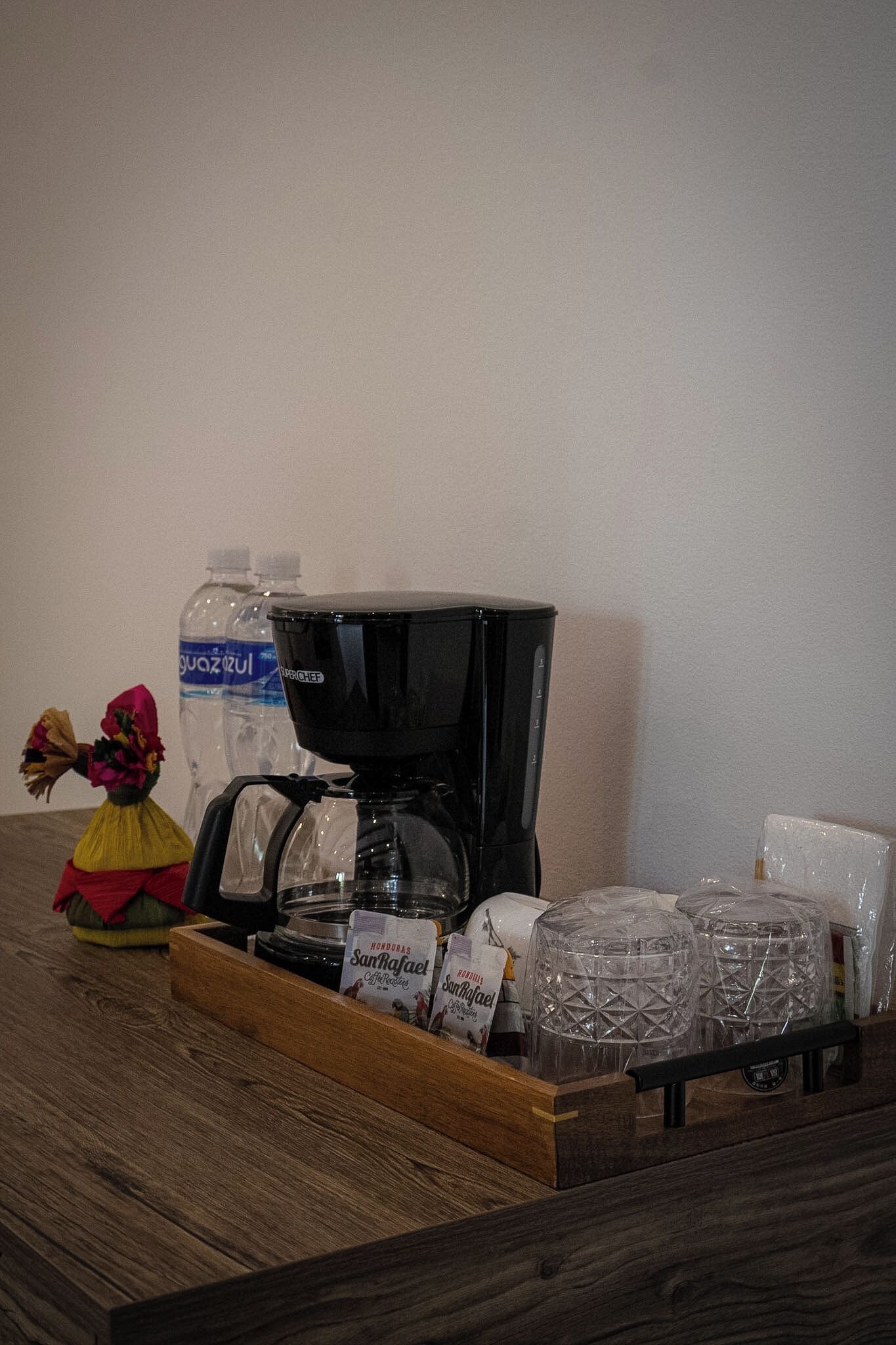 Uma cafeteira, uma garrafa de água e sachês de café sobre uma mesa de madeira.