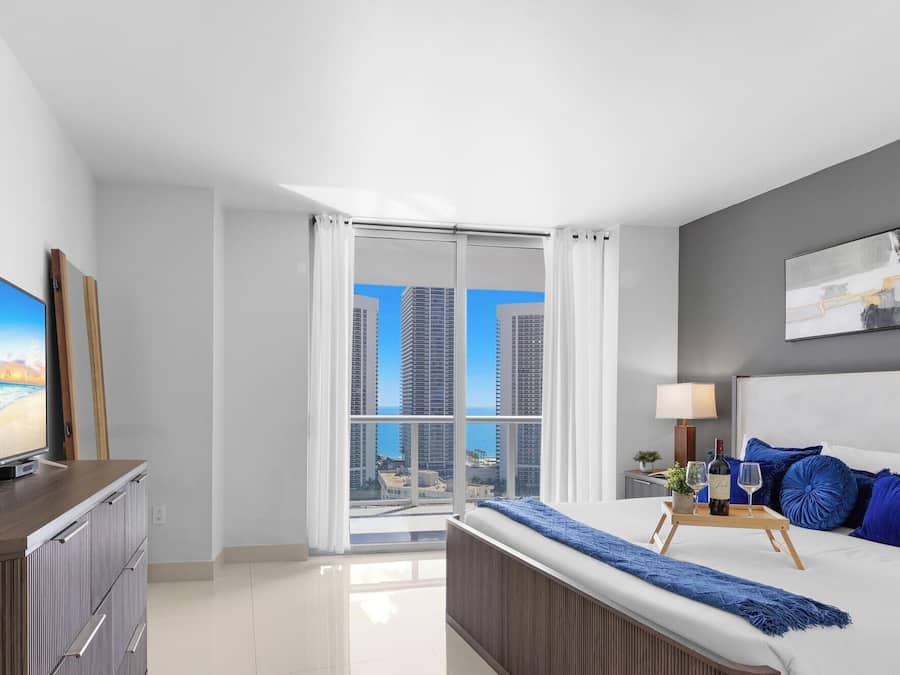 Quarto moderno com cama, televisão, escrivaninha e vista para edifícios altos.