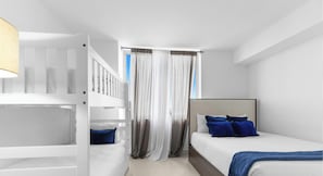 Quarto com beliche, uma cama de solteiro com almofadas azuis e uma janela com cortinas leves.