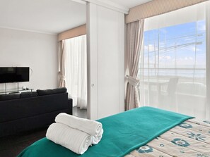 Quarto de hotel com cama, televisão, sofá e vista para o mar.