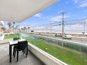 Varanda com guarda-corpo de vidro, vista para uma área gramada e uma estrada com carros.