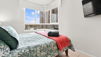 Quarto com cama, janela e vista de um prédio.