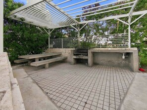 Um pátio externo com churrasqueira, área de estar e estrutura de pérgola.