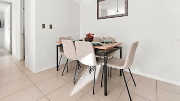 Uma sala de jantar com uma mesa posta para dois, cadeiras, um lustre pendente e um espelho fixado na parede.