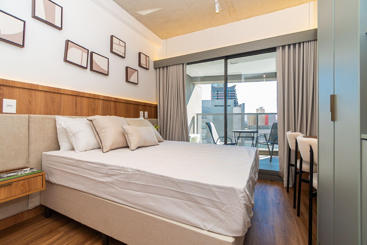 Quarto de hotel com cama, mesa de cabeceira, janela com cortinas e vista da cidade.