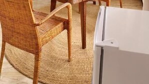 Quarto com mesa de jantar, cadeiras, geladeira e janela com cortinas.