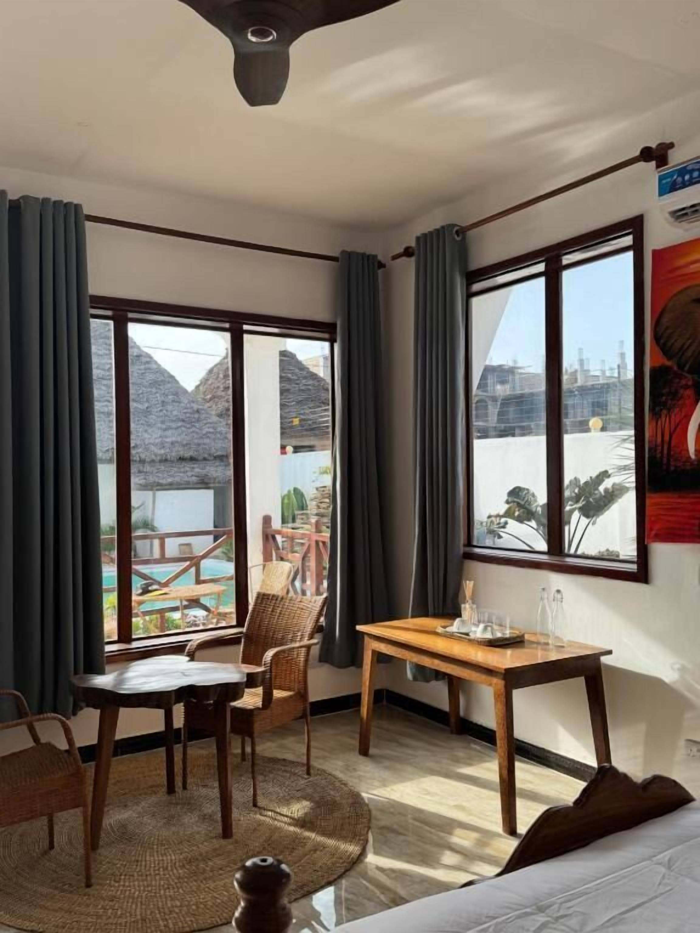 Quarto de hotel com cama, mesa de madeira, cadeira, vista para uma piscina e uma varanda.