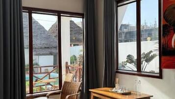 Quarto de hotel com cama, mesa de madeira, cadeira, vista para uma piscina e uma varanda.