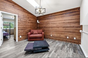 Um quarto com paredes de painel de madeira, um sofá vermelho, uma mesa de centro preta e um lustre.