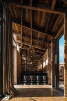 Um interior rústico com vigas de madeira aparente, um lustre pendurado e um espaço de bar com banquetas.