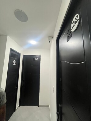Corredor com duas portas pretas, uma com a placa '101' e outra com a placa '102', e uma câmera de segurança no teto.