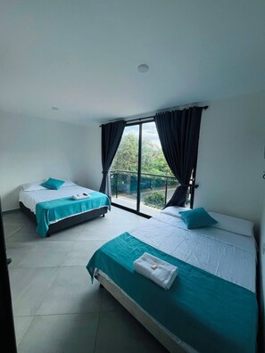 Quarto de hotel com duas camas, uma janela grande com cortinas e vista para área verde lá fora.