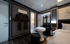Quarto de hotel moderno com uma cama, uma mesa redonda branca, um banquinho preto, uma pia branca e um espelho.