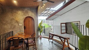 Quarto com teto de madeira, ventoinha no teto, mesa de jantar com cadeiras, um banco e um vaso com planta.