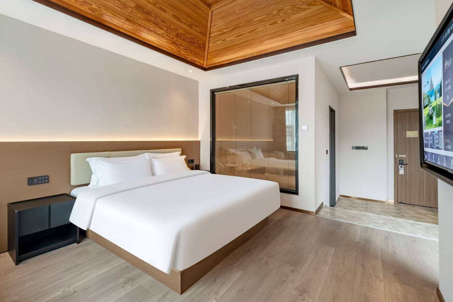 Quarto de hotel moderno com uma cama grande, teto de madeira, televisão e porta deslizante.