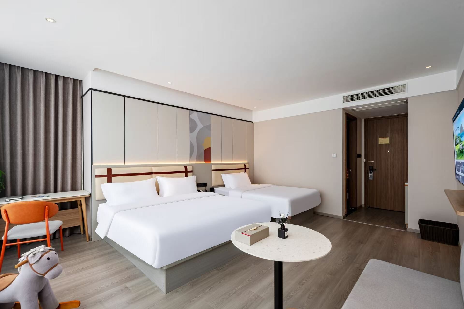 Quarto de hotel com cama de casal, escrivaninha, cadeira, mesa redonda pequena e um espelho grande.