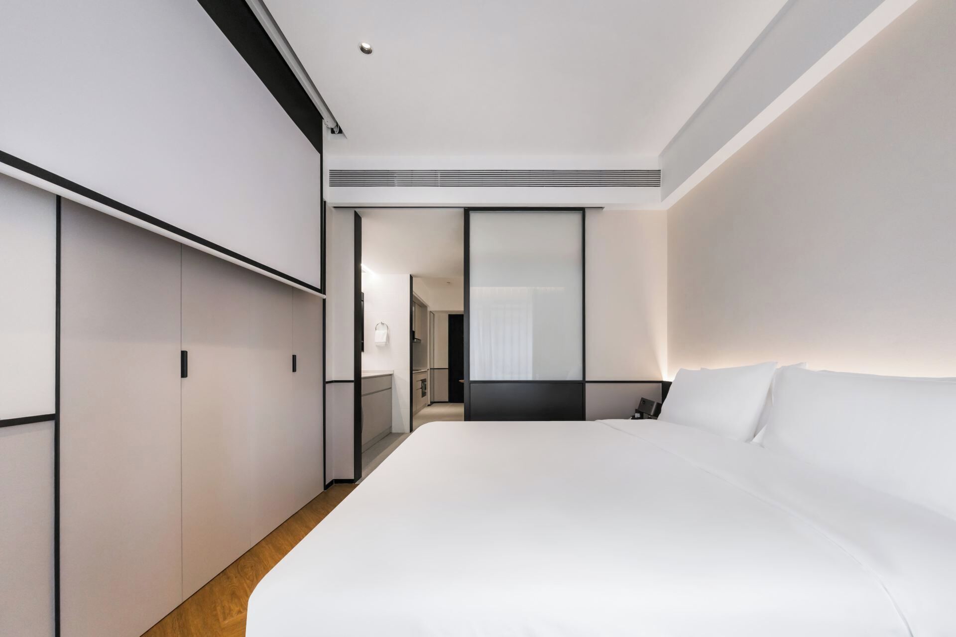 Quarto de hotel moderno com uma cama grande, um guarda-roupa e um banheiro visível através de uma porta.