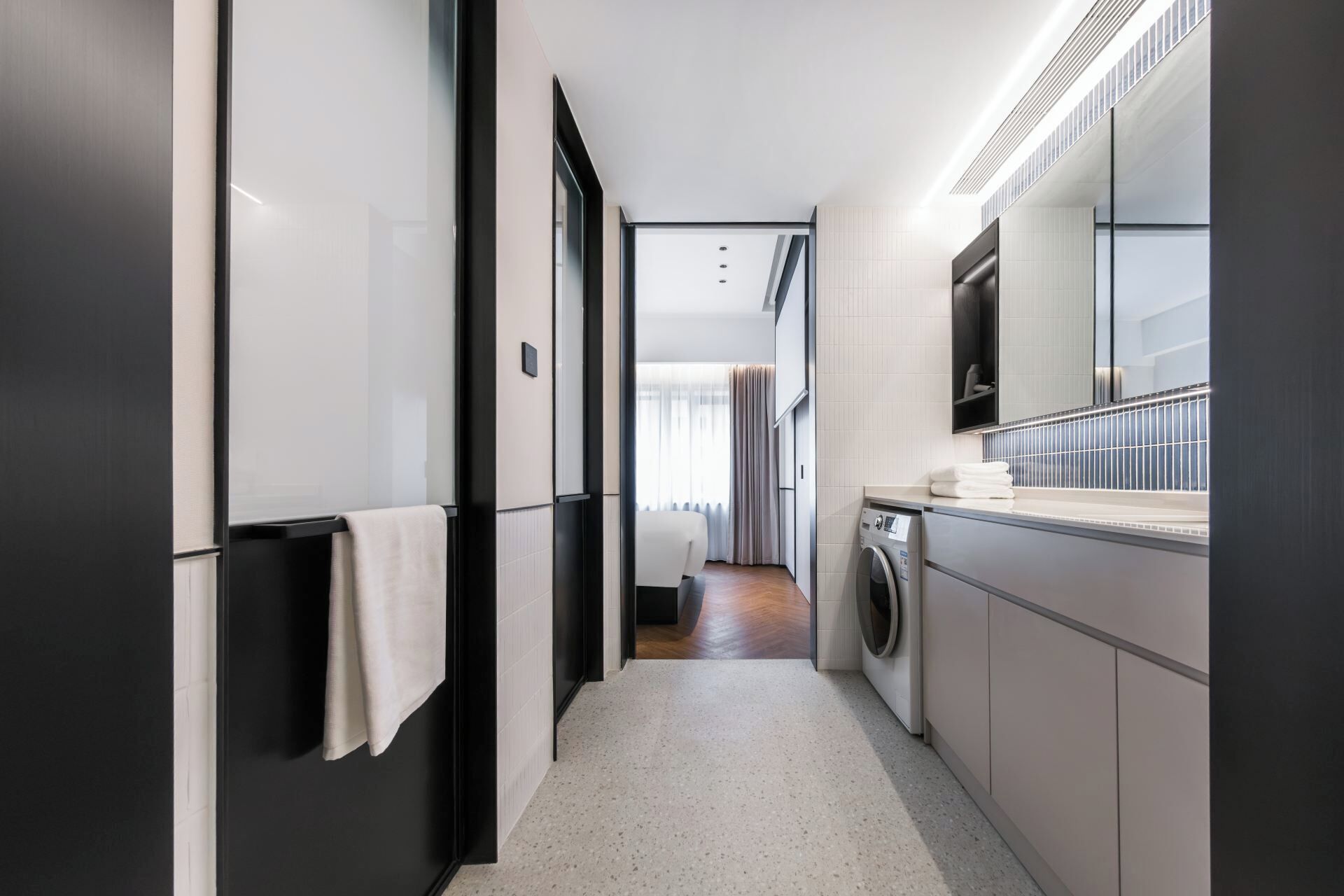 Um corredor estreito dá para uma cozinha moderna com máquina de lavar, bancada e um espelho grande.
