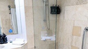 Uma casa de banho moderna com cabine de duche em vidro, banheira e lavatório com artigos de higiene pessoal.