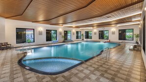 Piscina interna com chão de azulejos, teto de madeira e amplas janelas.