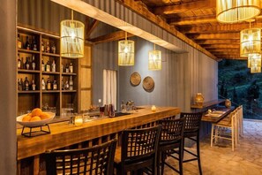 Uma área de bar com móveis de madeira, prateleiras com garrafas e luminárias pendentes.