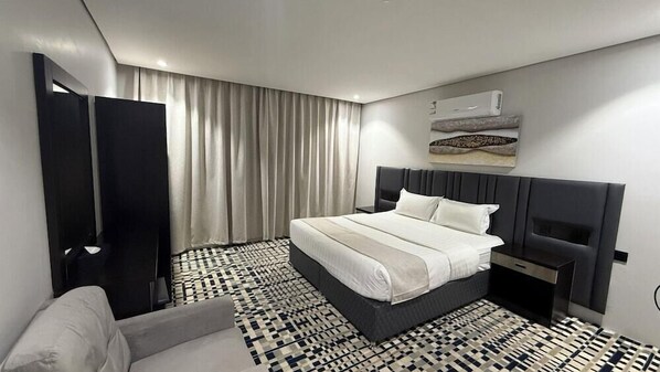 Quarto de hotel moderno com uma cama grande, uma mesinha de cabeceira, uma cadeira e um tapete estampado.