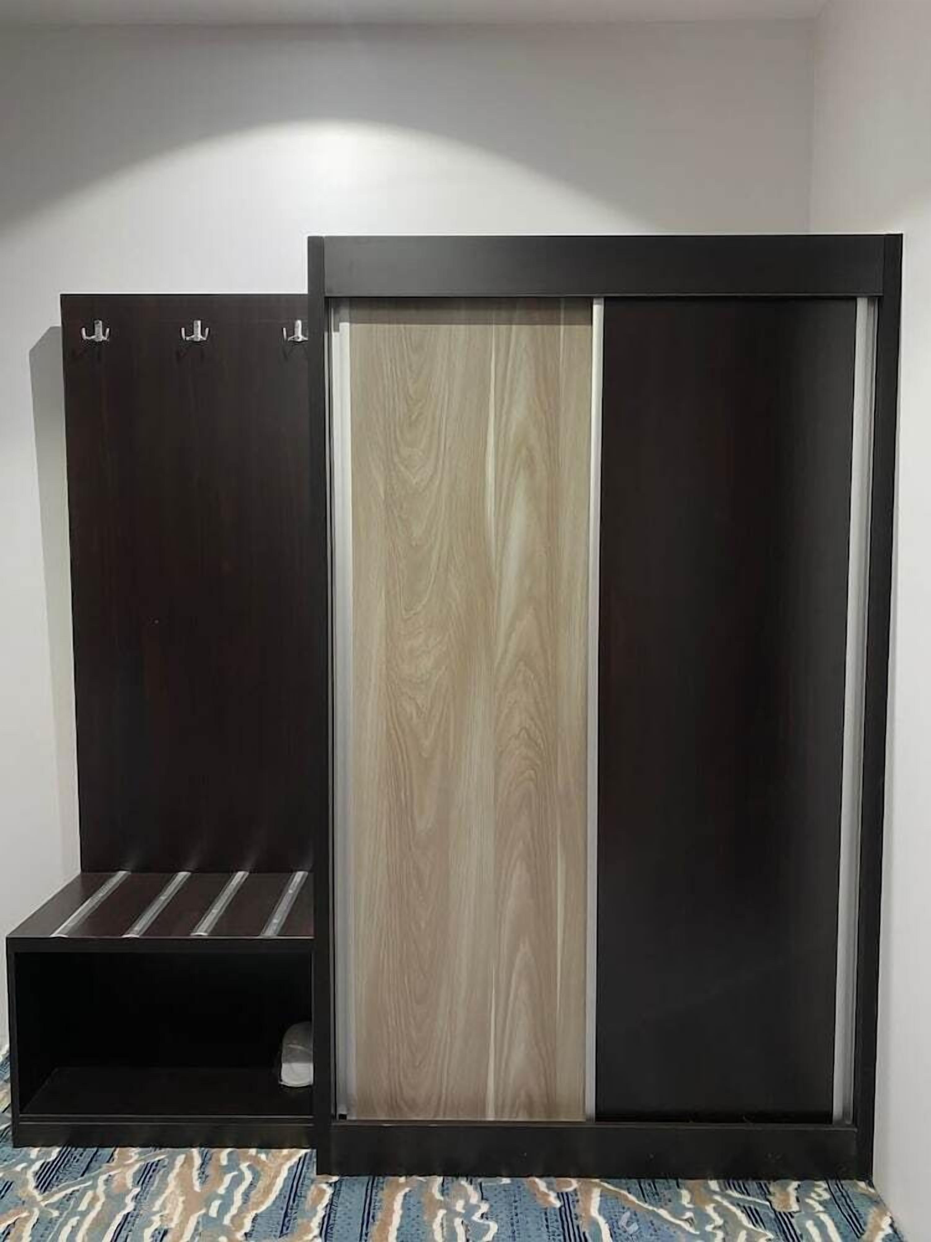 A room with a dark-colored wardrobe, a wooden panel, and a shelf unit.
