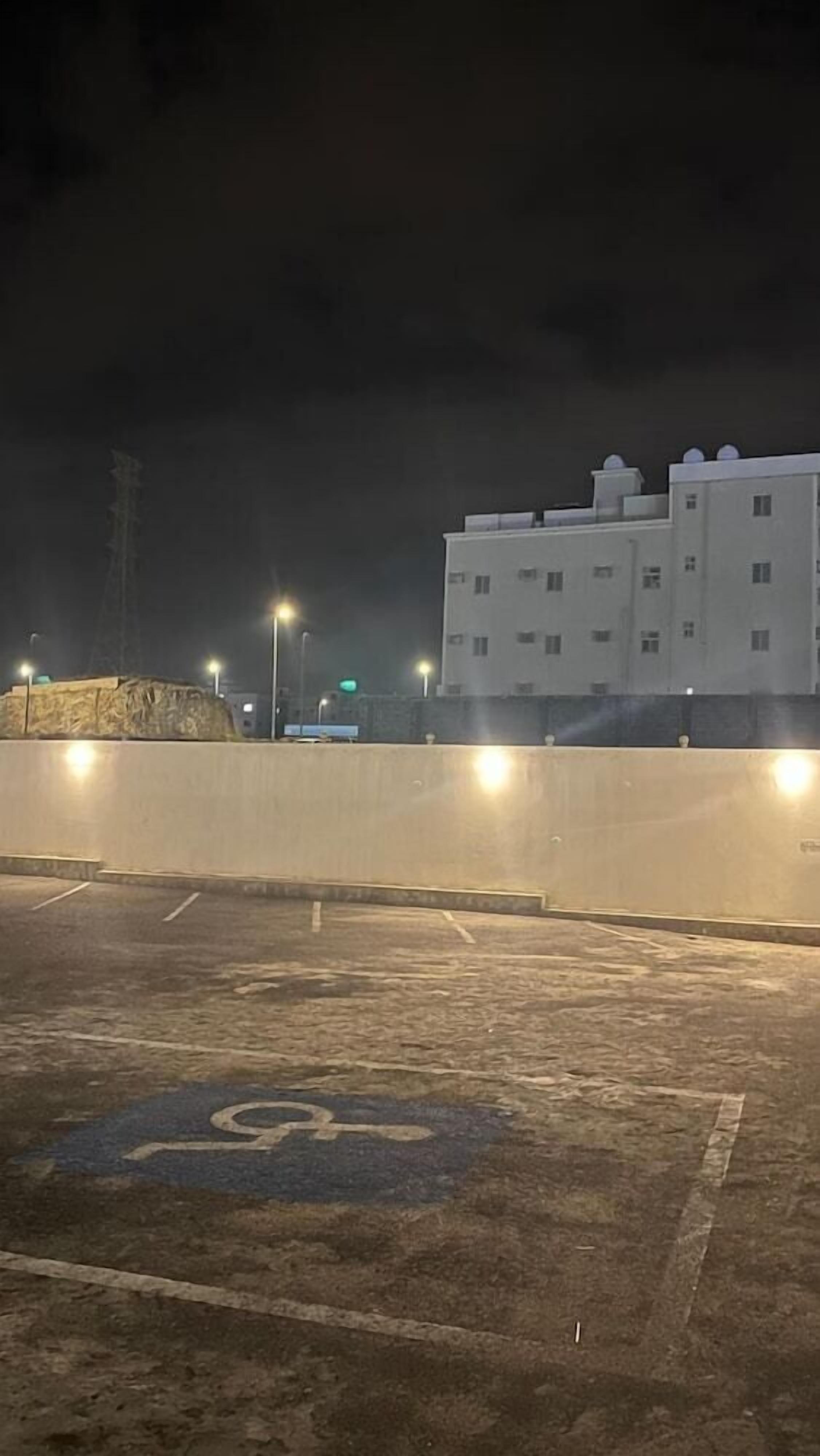 A parking area with a handicap parking symbol, a building in the background, and streetlights.