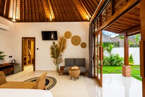 Um interior moderno com teto de madeira, televisão de tela plana, sofá cinza e uma janela grande com vista para um jardim.