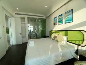 Quarto de hotel com cama, closet amplo, chuveiro envidraçado e obras de arte na parede.