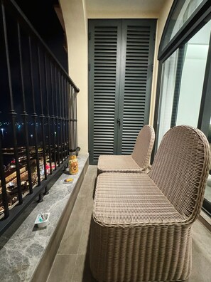 Varanda com móveis de vime, uma porta fechada e vista para a cidade à noite.