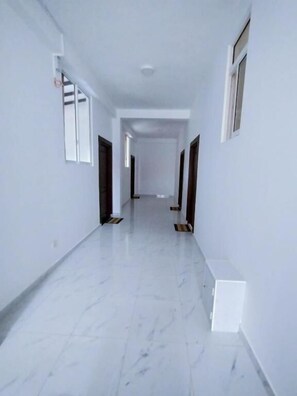 Um corredor com paredes brancas e chão de mármore, que leva a uma porta no final.