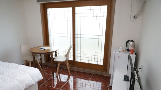 Quarto de hotel com cama, escrivaninha com cadeira, cafeteira e televisão.